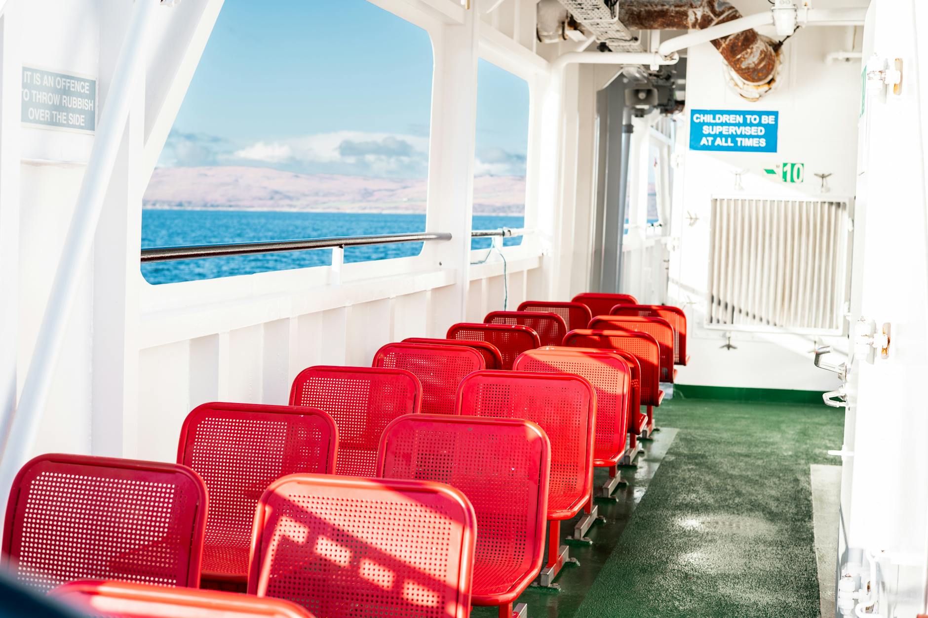 Empty red seats on a ferry deck overlooking scenic waters